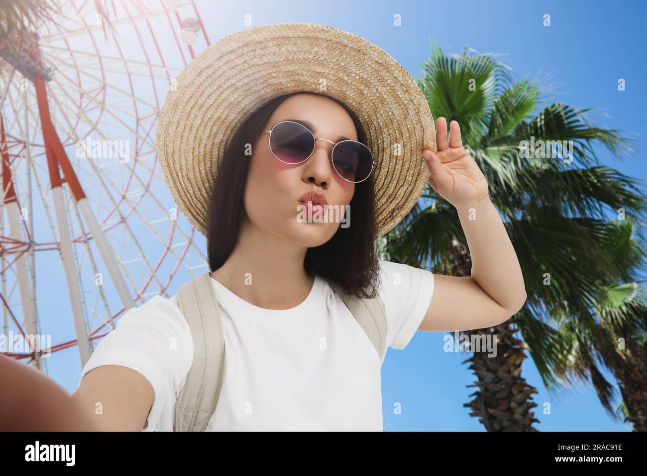 Smiling Young Woman In Sunglasses And Straw Hat Taking Selfie Near