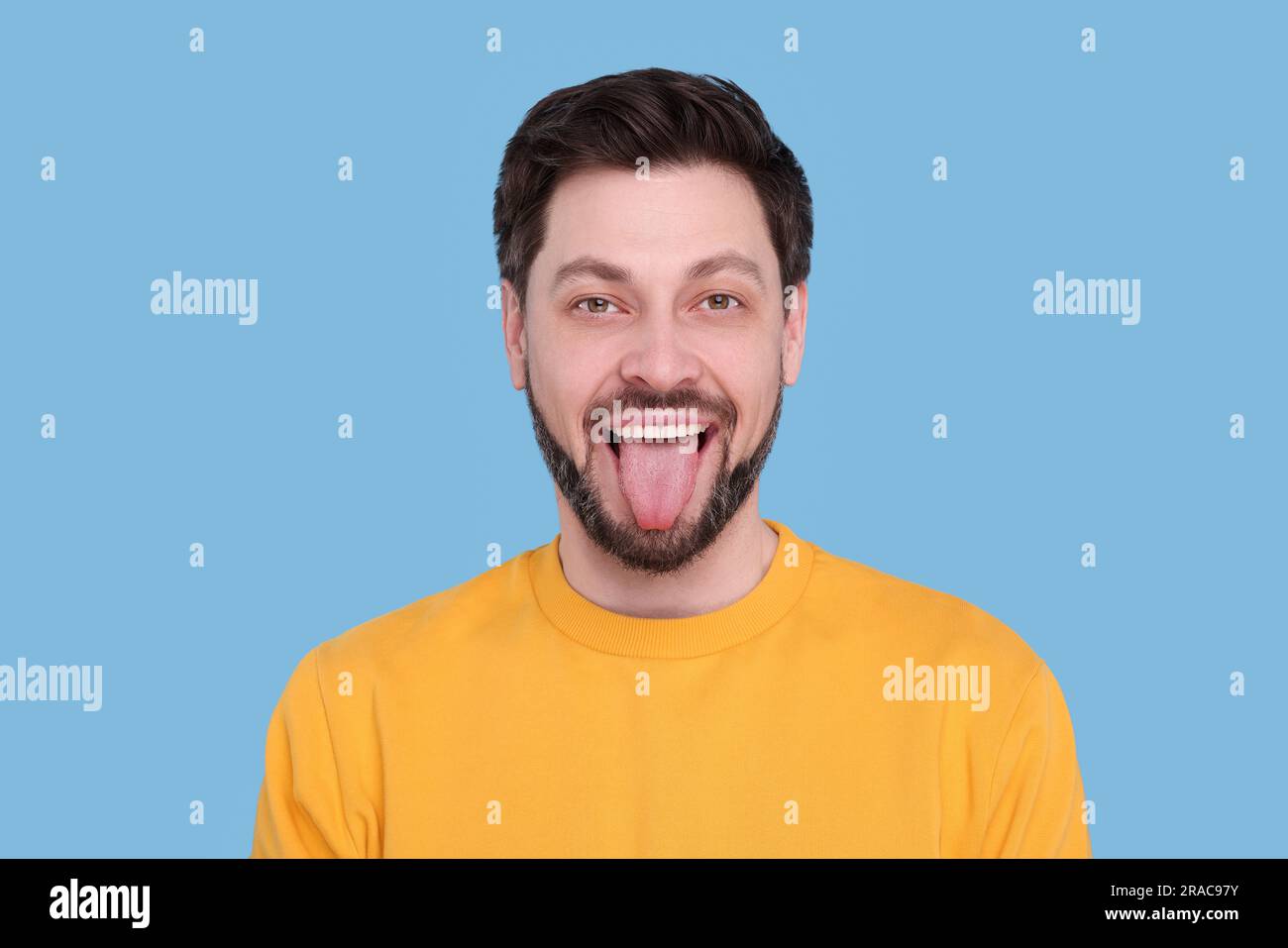 Happy man showing his tongue on light blue background Stock Photo - Alamy