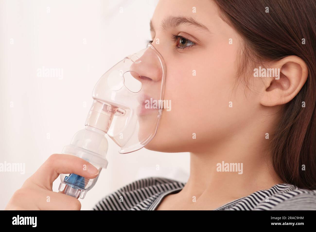 Cute girl using nebulizer for inhalation on white background, closeup ...