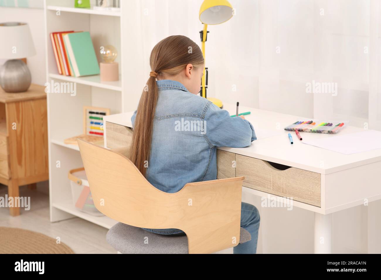 Cute little girl drawing with markers at desk in room. Home workplace ...