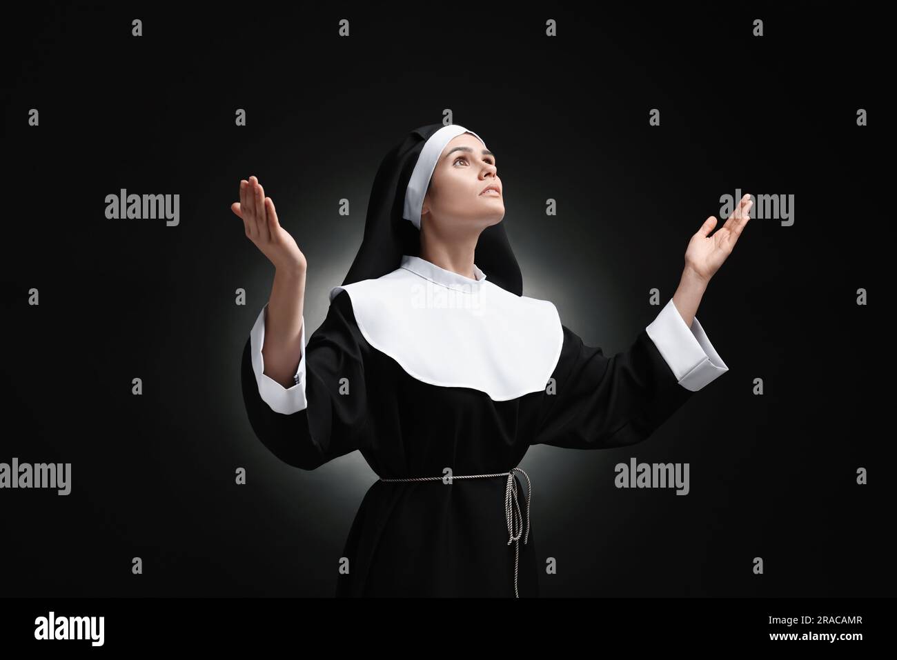 Nun praying to God on black background Stock Photo - Alamy