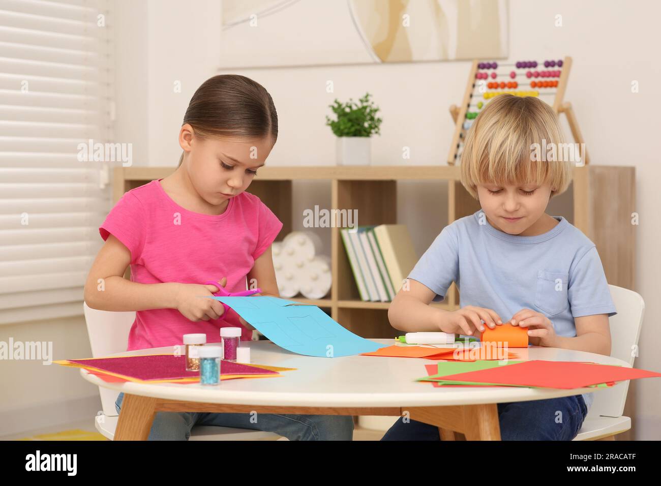 Cute children cutting colorful paper at desk in room. Home workplace ...