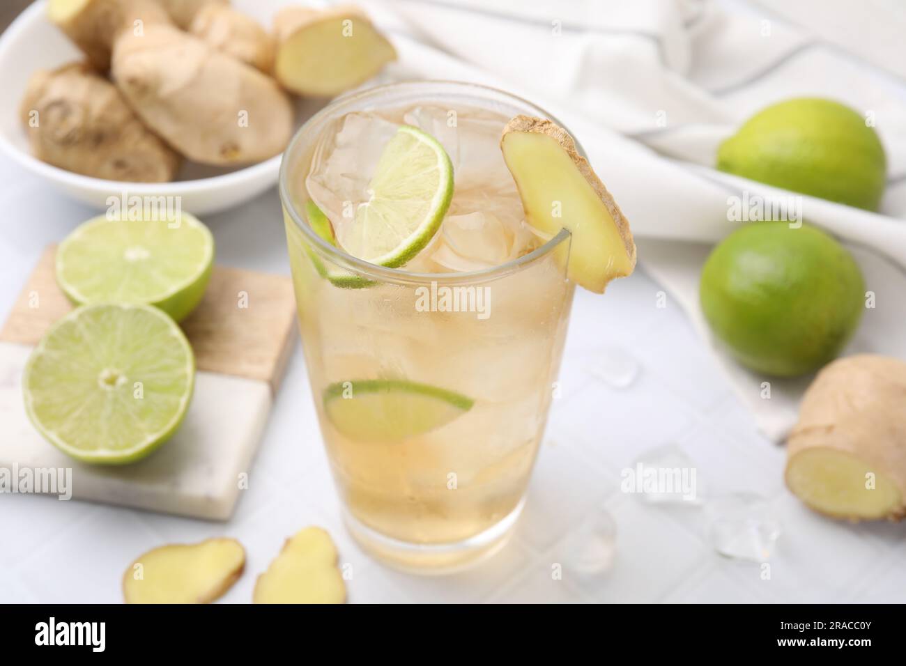 Glass of tasty ginger ale with ice cubes and ingredients on white tiled ...
