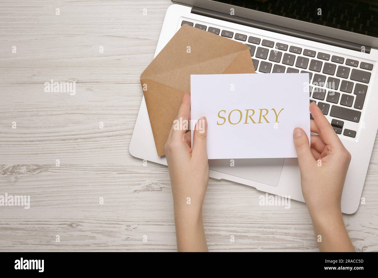 Apology. Woman holding card with word Sorry near envelope and laptop at ...