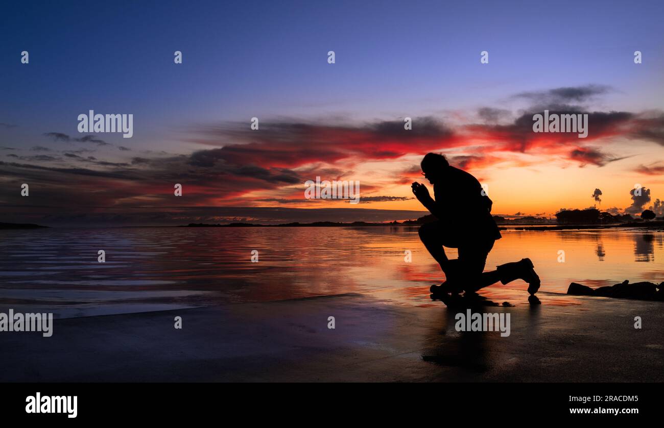 A man on his kneeeling in prayer to God of all creation. As the setting ...