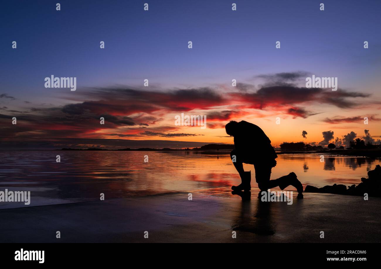 A man on his kneeeling in prayer to God of all creation. As the setting ...