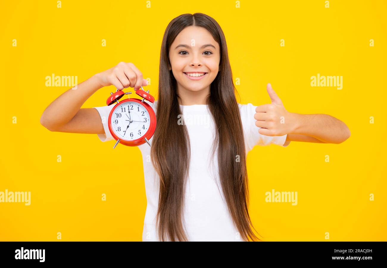 Happy teenager portrait. Teen girl holding clock over yellow background ...