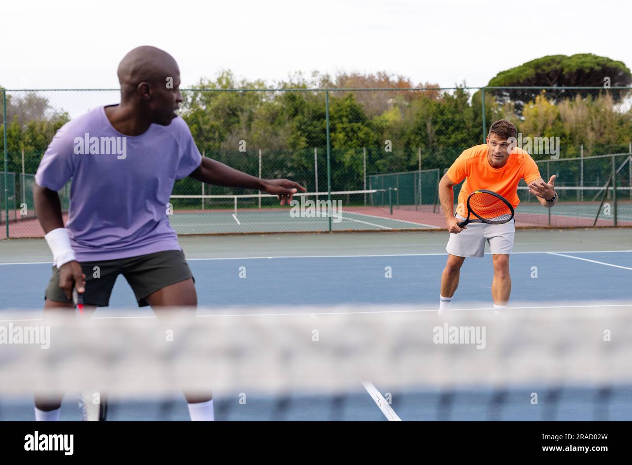 Diverse male tennis players playing doubles on outdoor court Stock ...