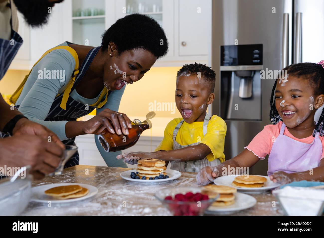 Cheerful african american mother pouring honey on pancakes while ...