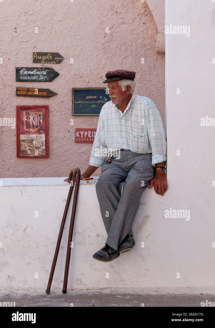 An elderly Greek man sitting on a low wall observes the landscape on ...