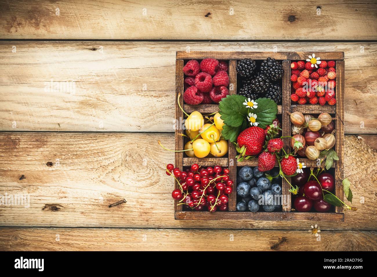 Mix of fresh berries with leaves in vintage wooden box on rustic wooden ...