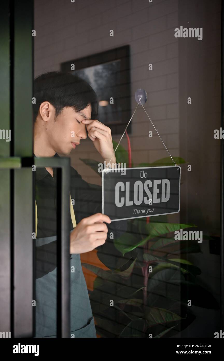 Depressed young coffee shop owner closing his coffee shop, closing down ...
