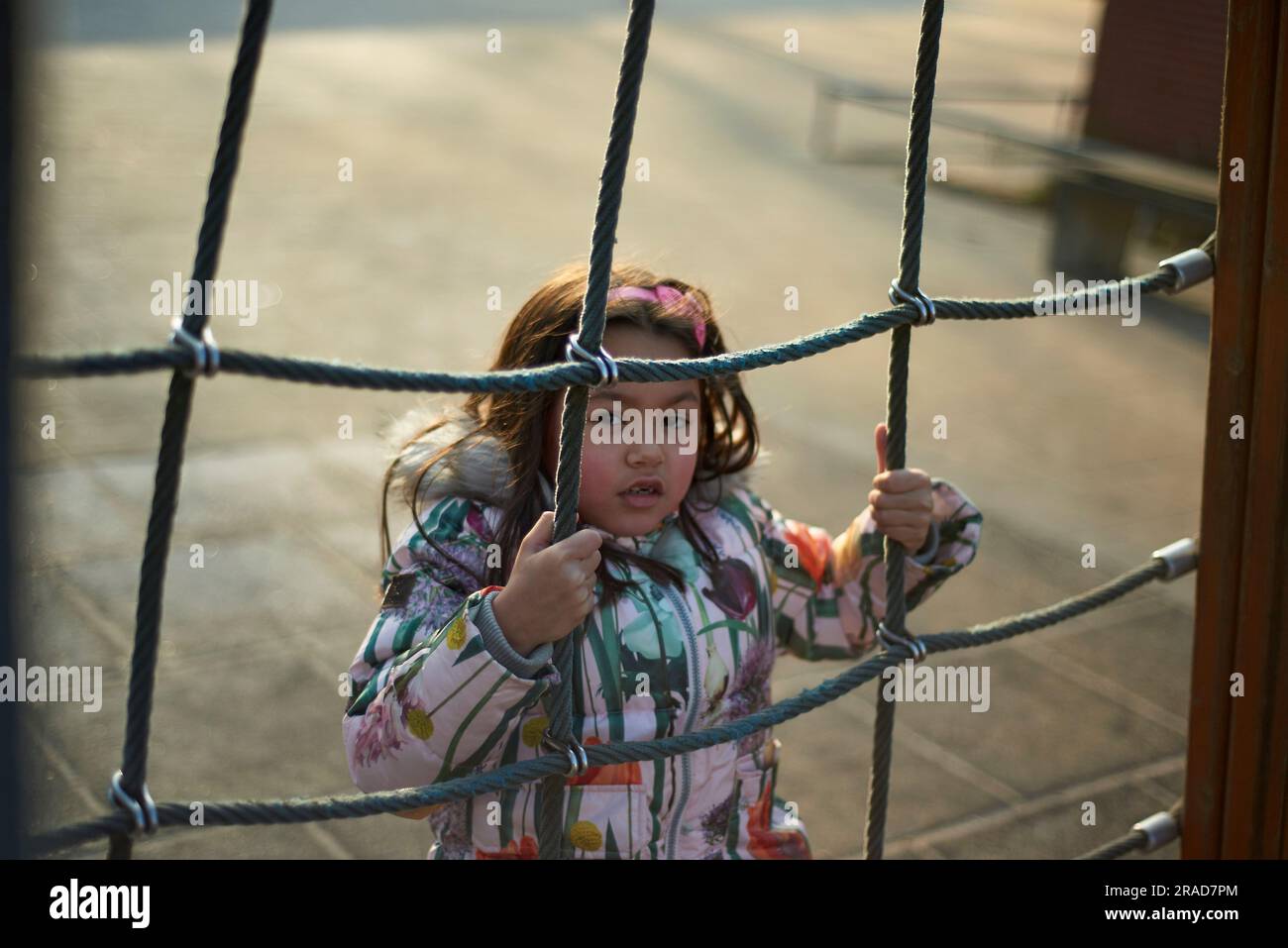 Portrait of a young Asian girl climbing in a climbing frame at school ...
