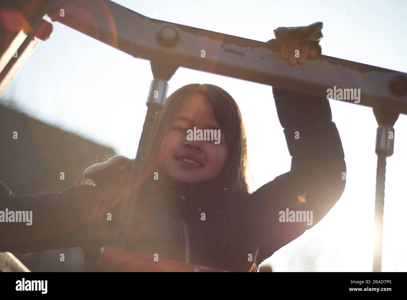 Portrait of a young Asian girl climbing in a climbing frame at school ...