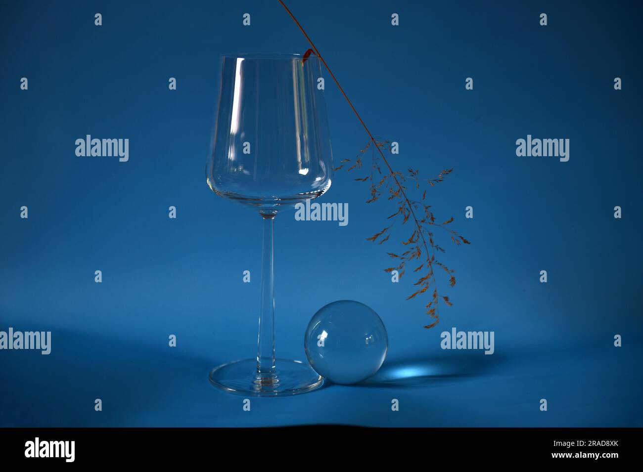 Empty glass, glass ball and dried straw against blue background Stock ...