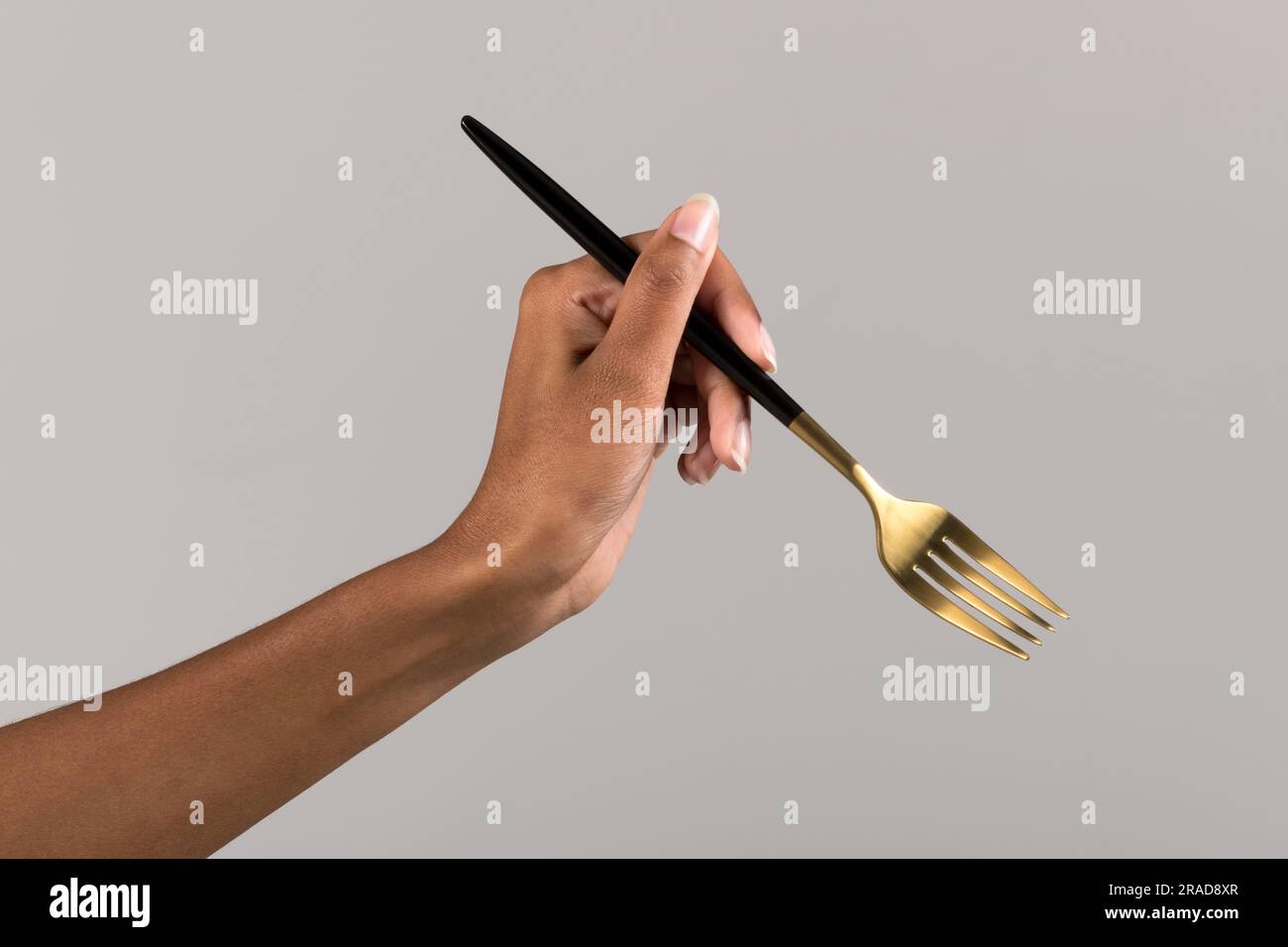 Hand of anonymous black female holding golden fork with black handle ...