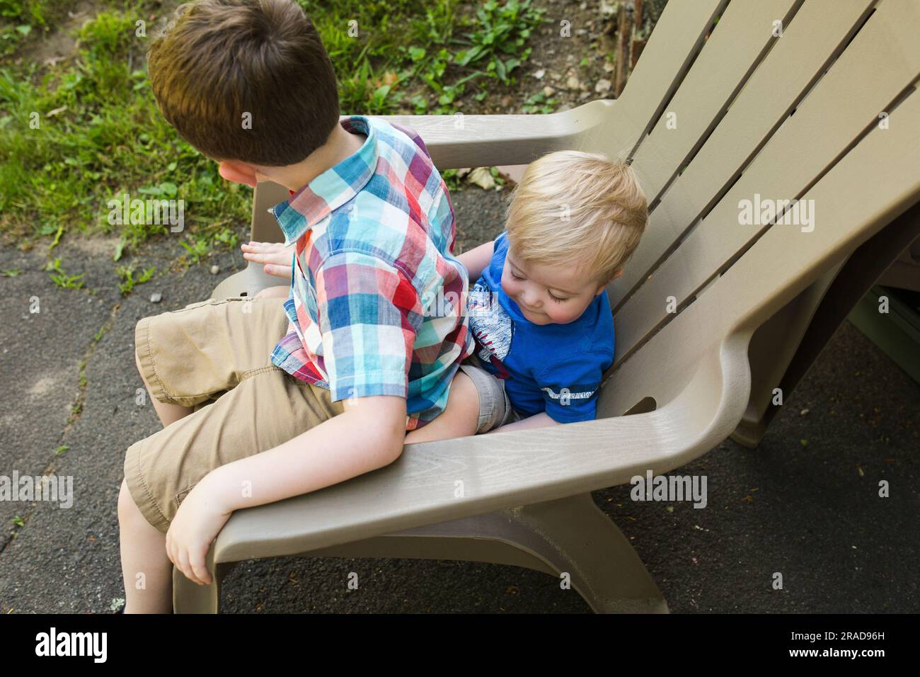 Two brothers sit in same chair outdoors during summer in backyard Stock ...