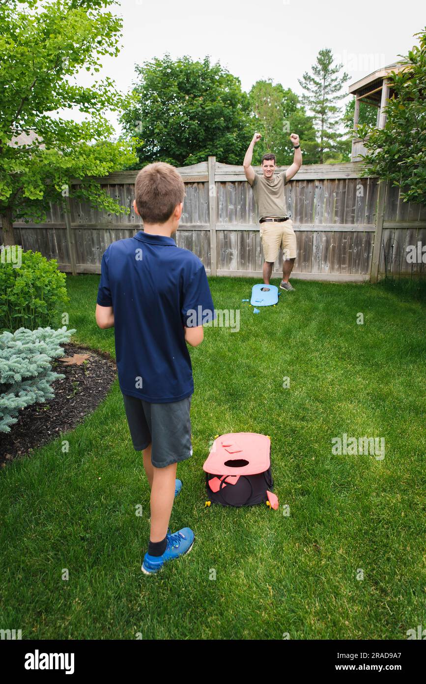 Father and son having fun playing corn hole game together in backyard ...