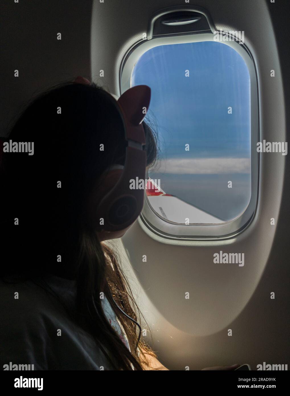 Child girl observing the sky from the window of an aircarft. She has ...