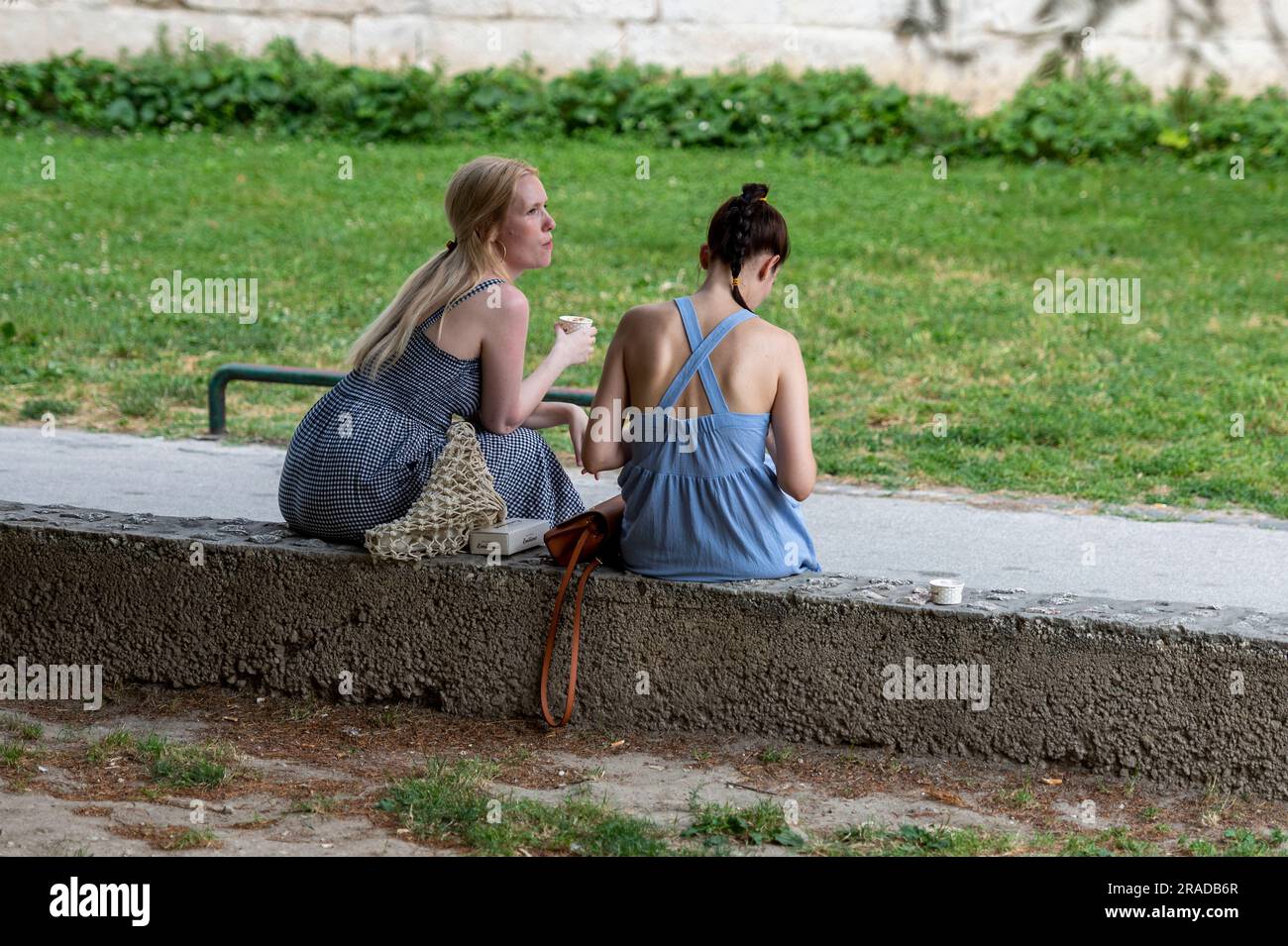 two young women sitting on a wall together in a park in split, croatia ...