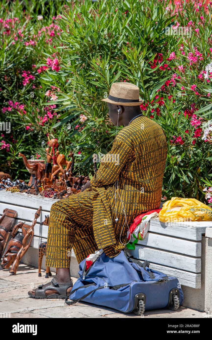 street trader sitting on a wall displaying his wares in the holiday ...