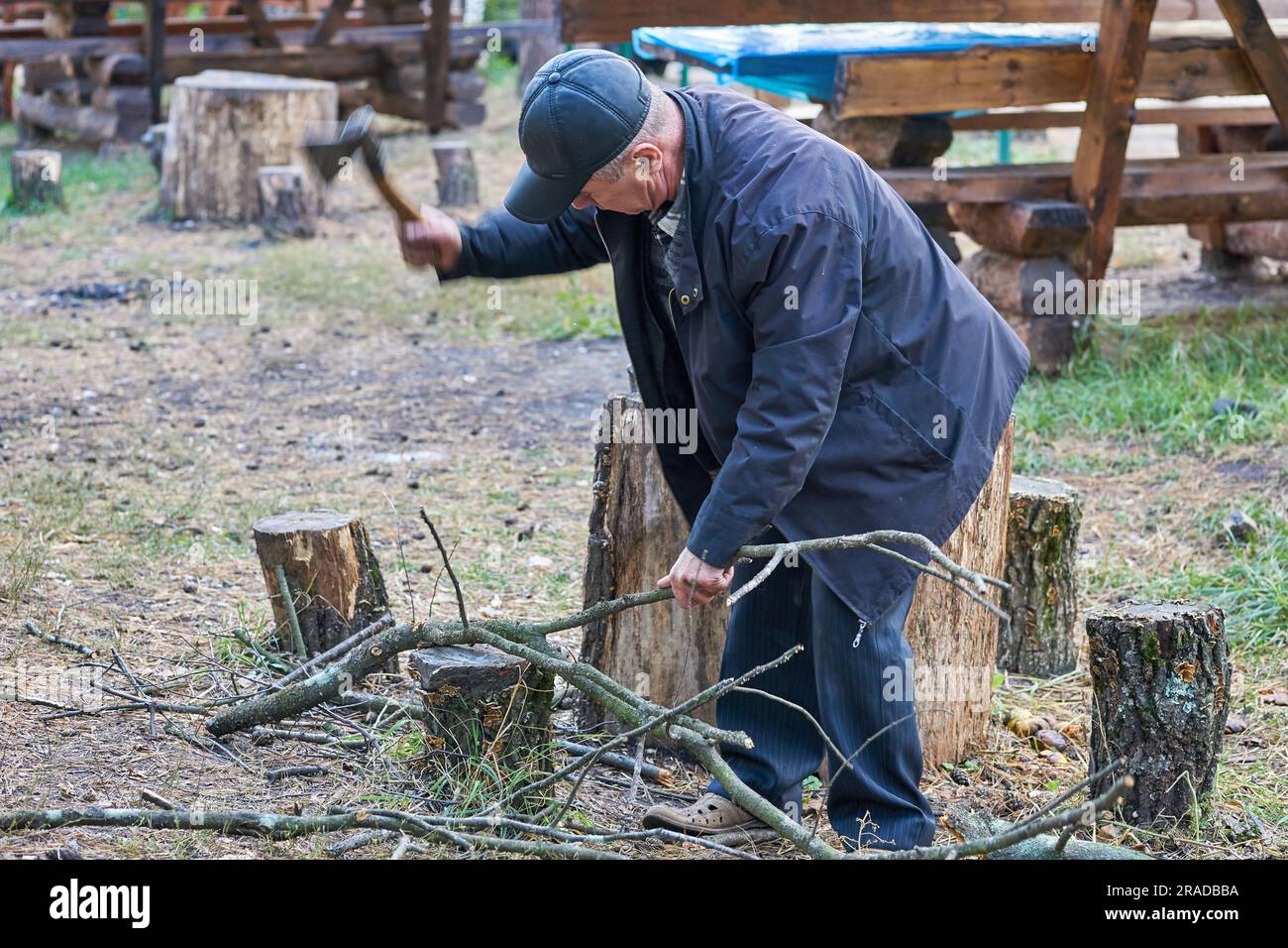 Elderly retired man chopping firewood with an ax, cooking grilled food ...