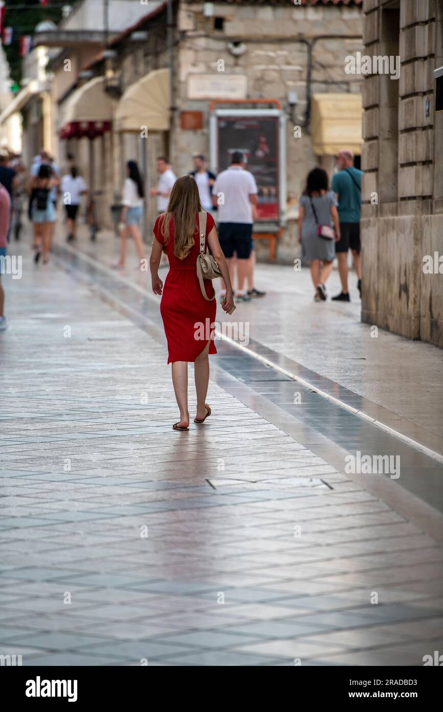 attractive young woman with long hair wearing red summer dress walking alone through the old ...