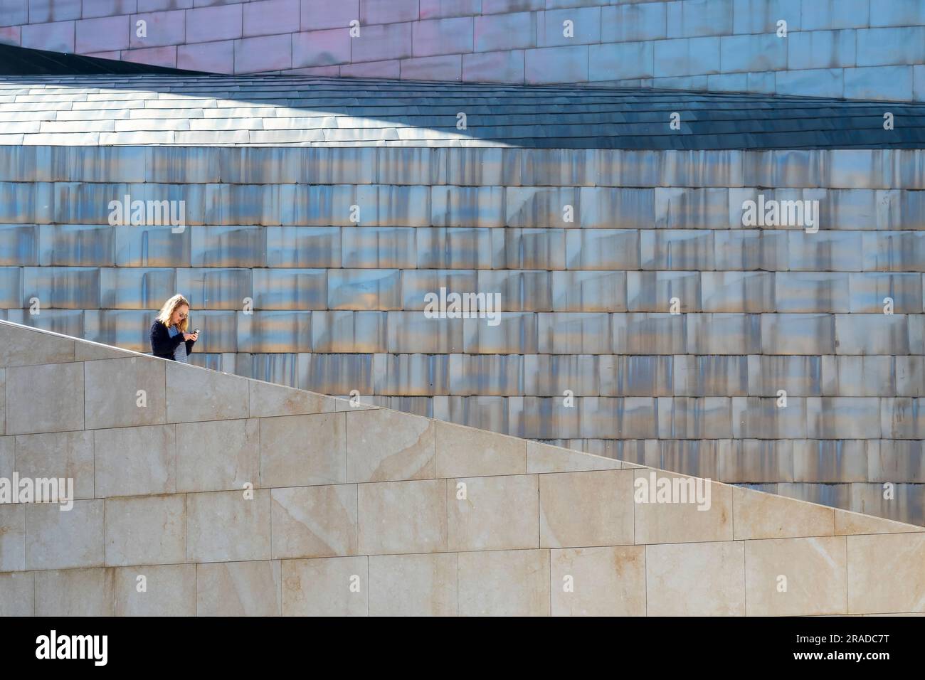 Young woman walking past the titanium façade of the Guggenheim Museum ...