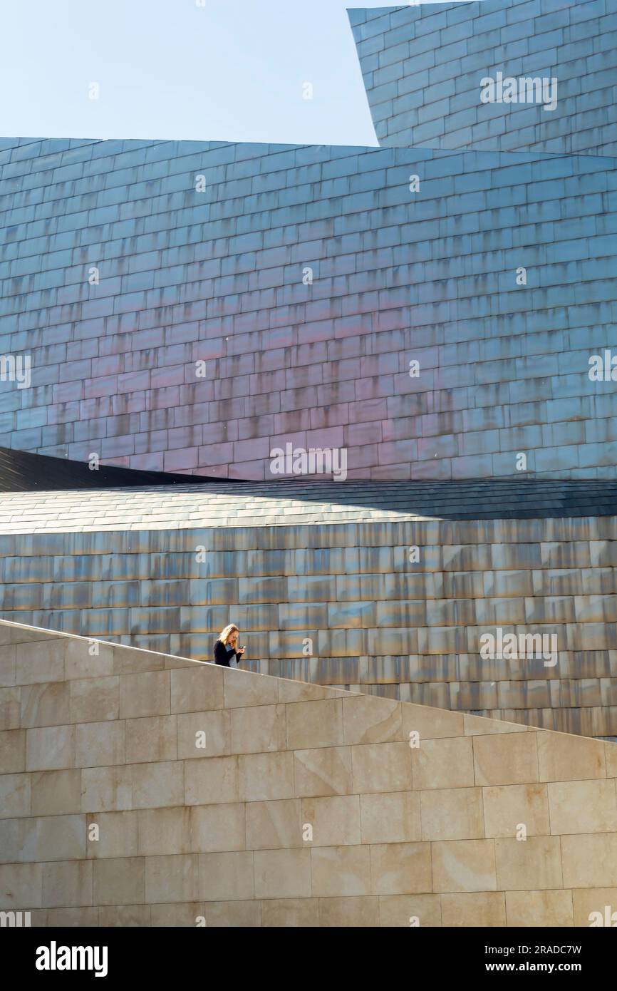 Young woman walking past the titanium façade of the Guggenheim Museum ...