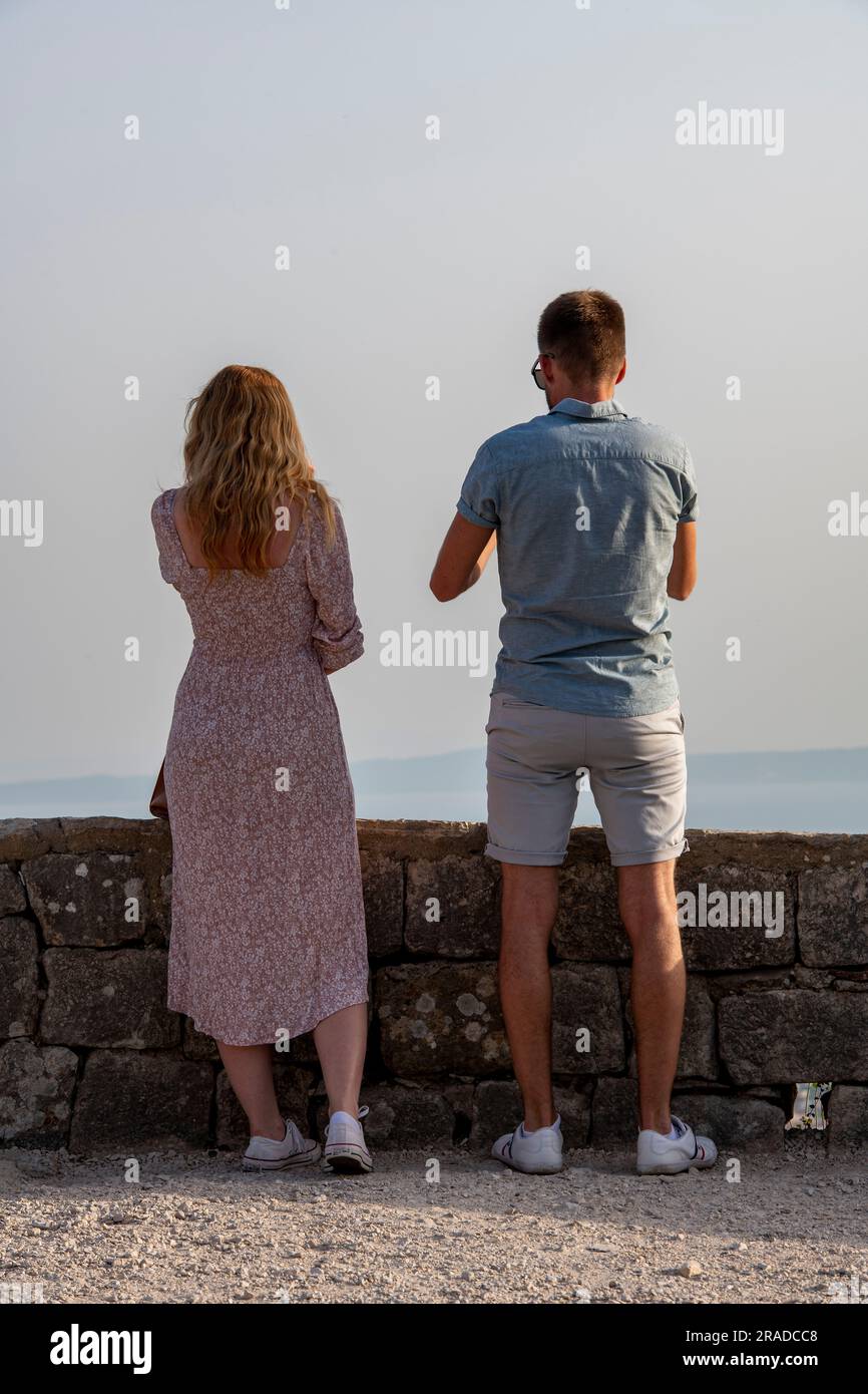 young man and woman standing next to a low wall together looking out ...