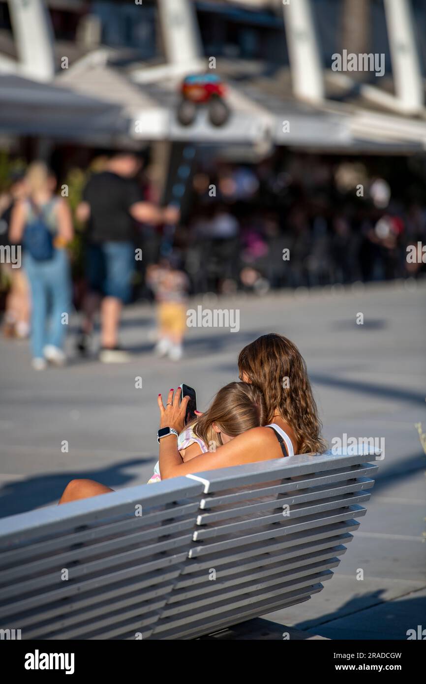 mother and child sitting on a bench in the warm mediterranean sunshine ...