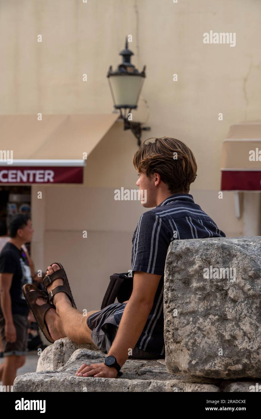 young man sitting on a wall relaxing in the early evening mediterranean ...