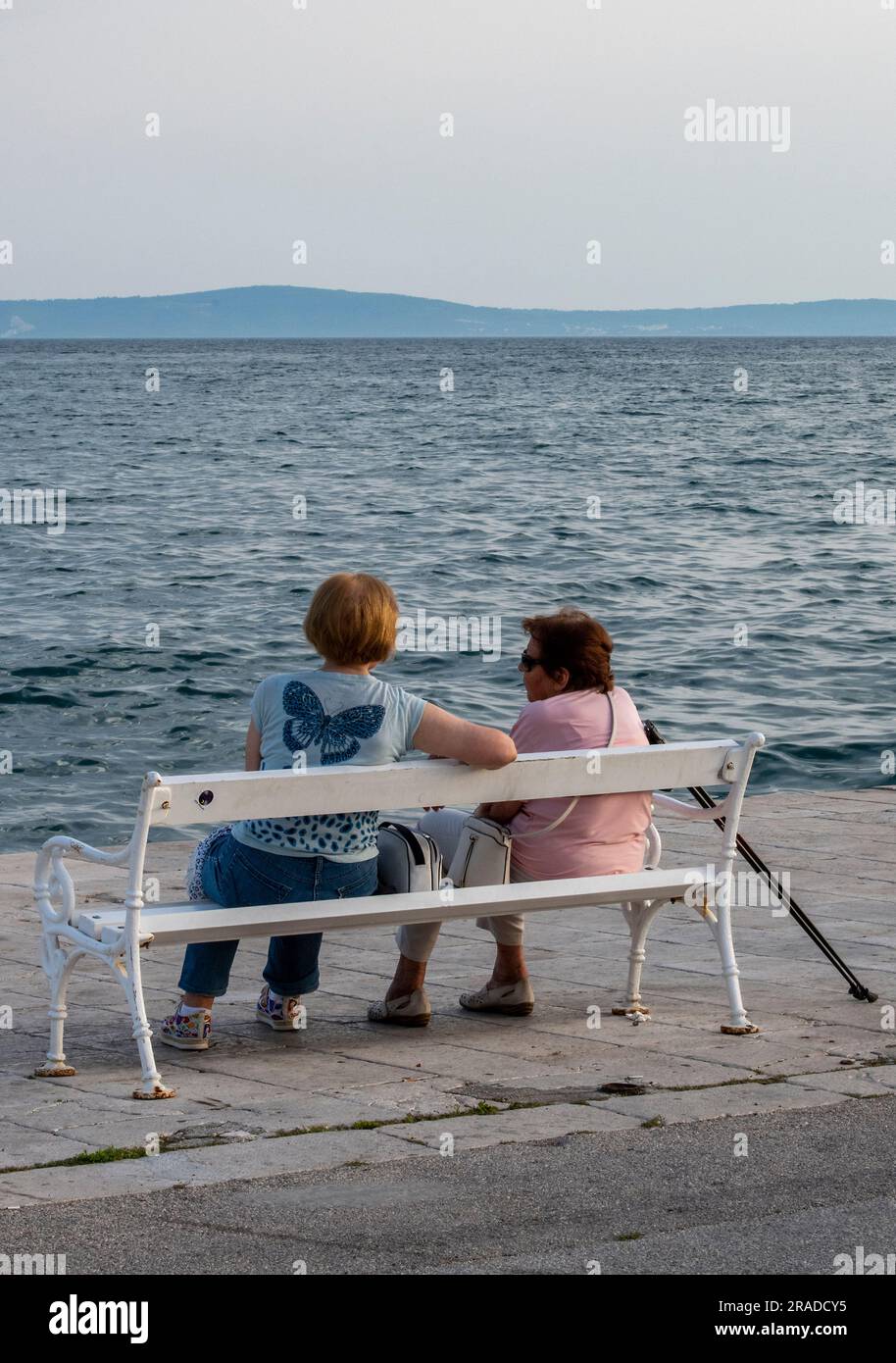 two older ladies sitting on a bench at the seaside, two elderly retired ...