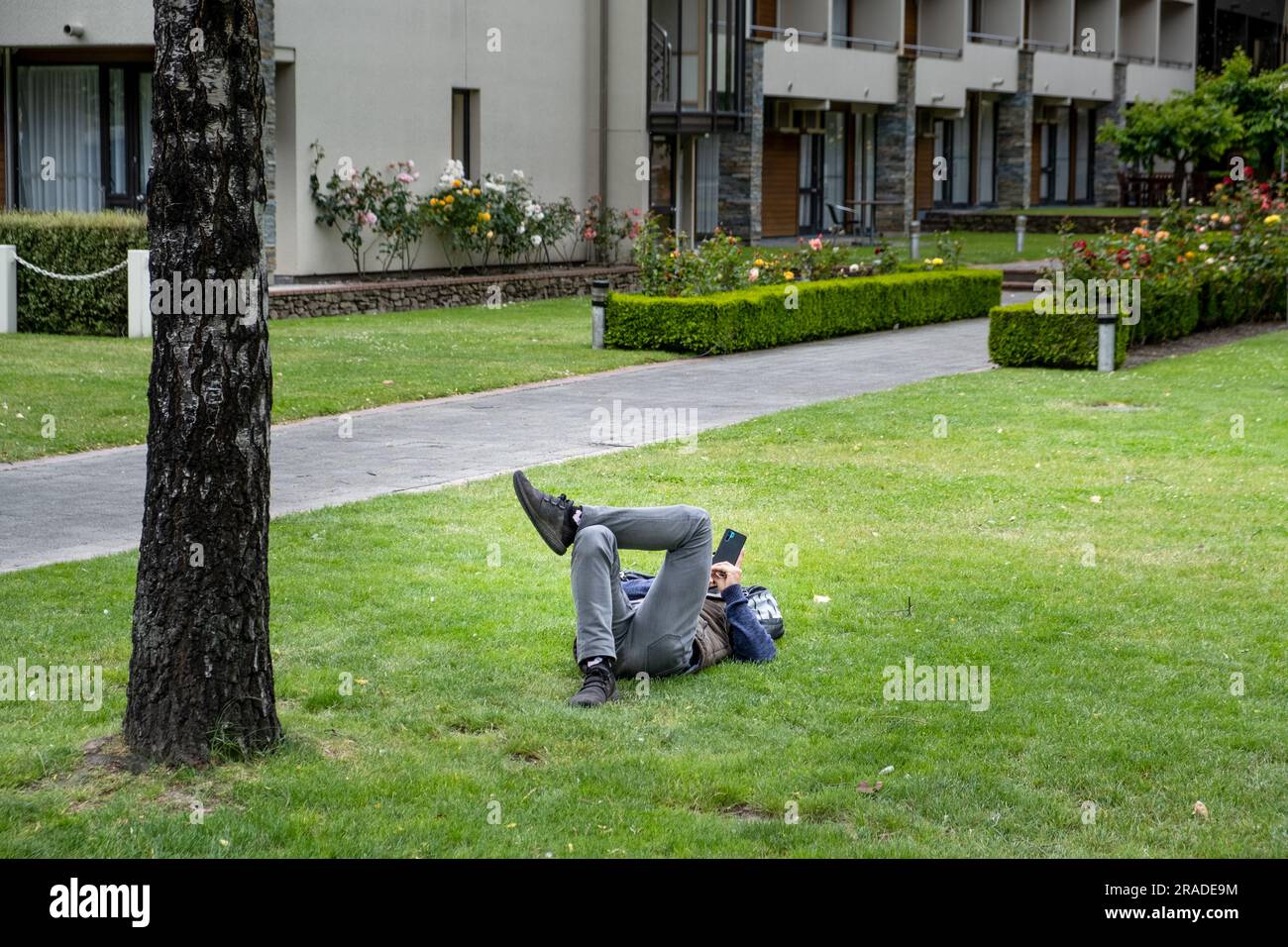 An anonymous man lying on grass scrolling on his mobile phone in ...