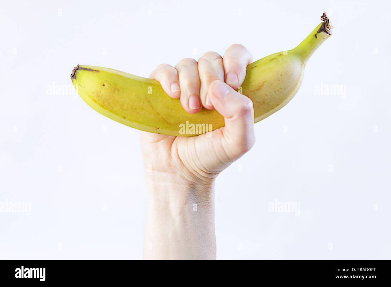 A female hand holding a ripe fresh yellow banana isolated on a white ...