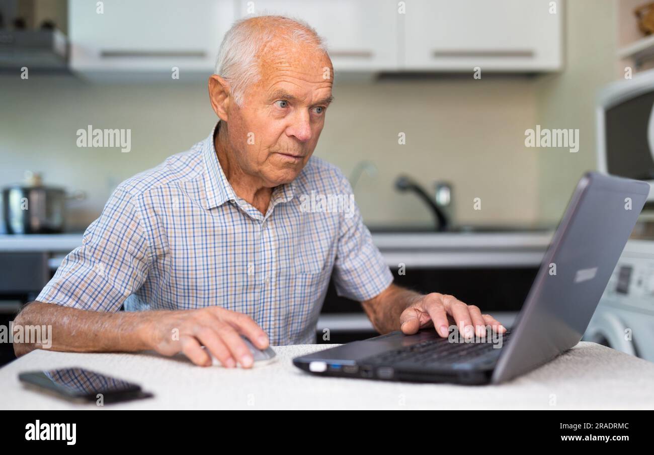 Elderly man is carefully studying the capabilities of a laptop Stock ...