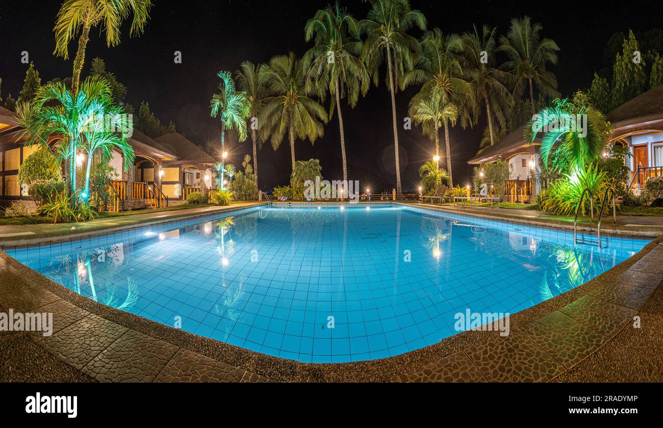 Night shot over illuminated swimming pool in tropical environment with ...