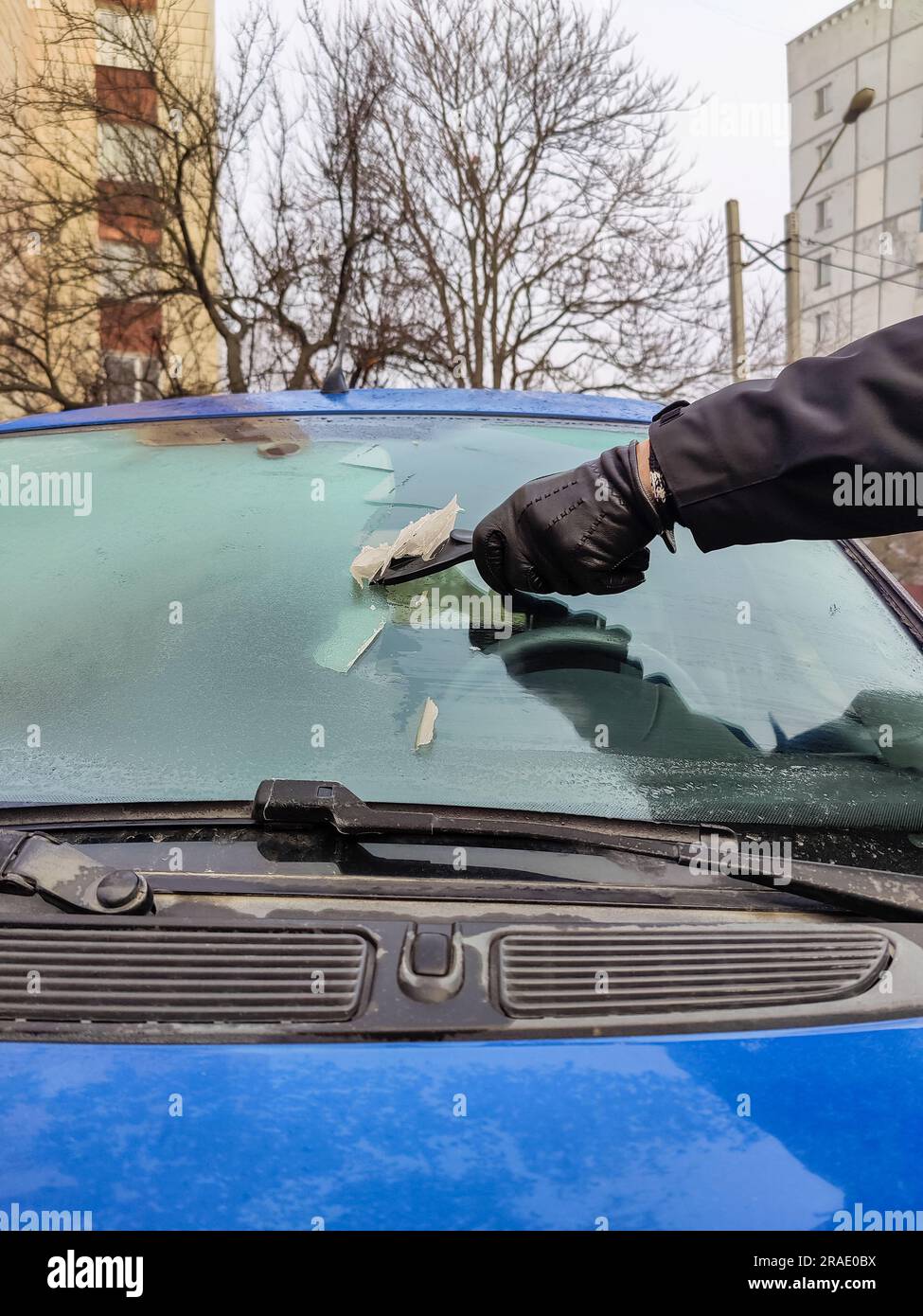Man scrapes hoarfrost with a plastic scraper from the side window of a ...