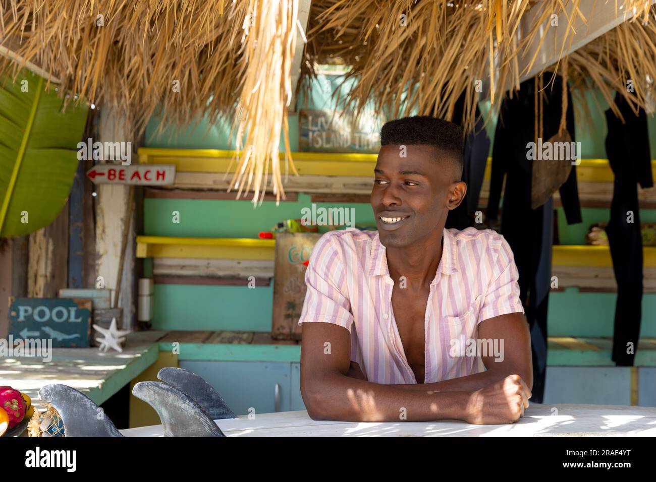 Happy african american man sitting behind counter of surf hire beach ...