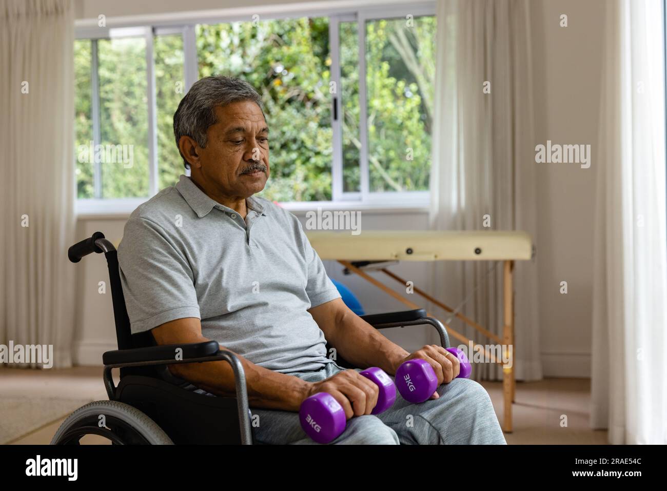 Determined senior biracial male patient in wheelchair using dumbbells ...