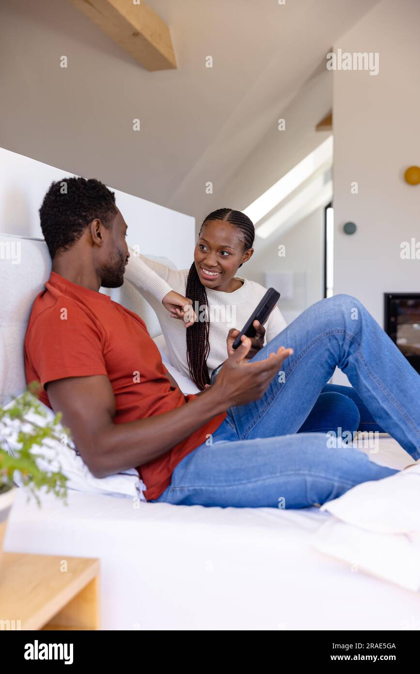 Happy african american couple using smartphones and talking lying on ...
