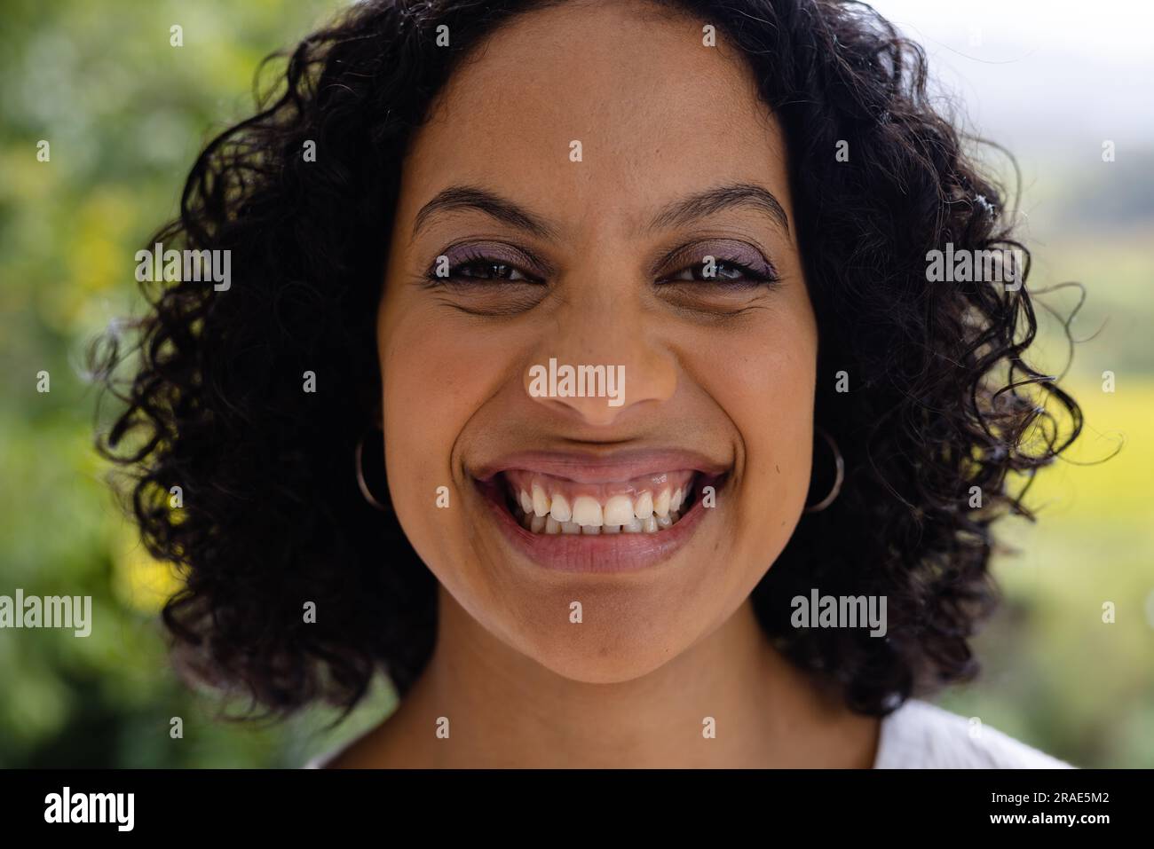 Portrait of smiling biracial woman with curly dark hair in front of ...