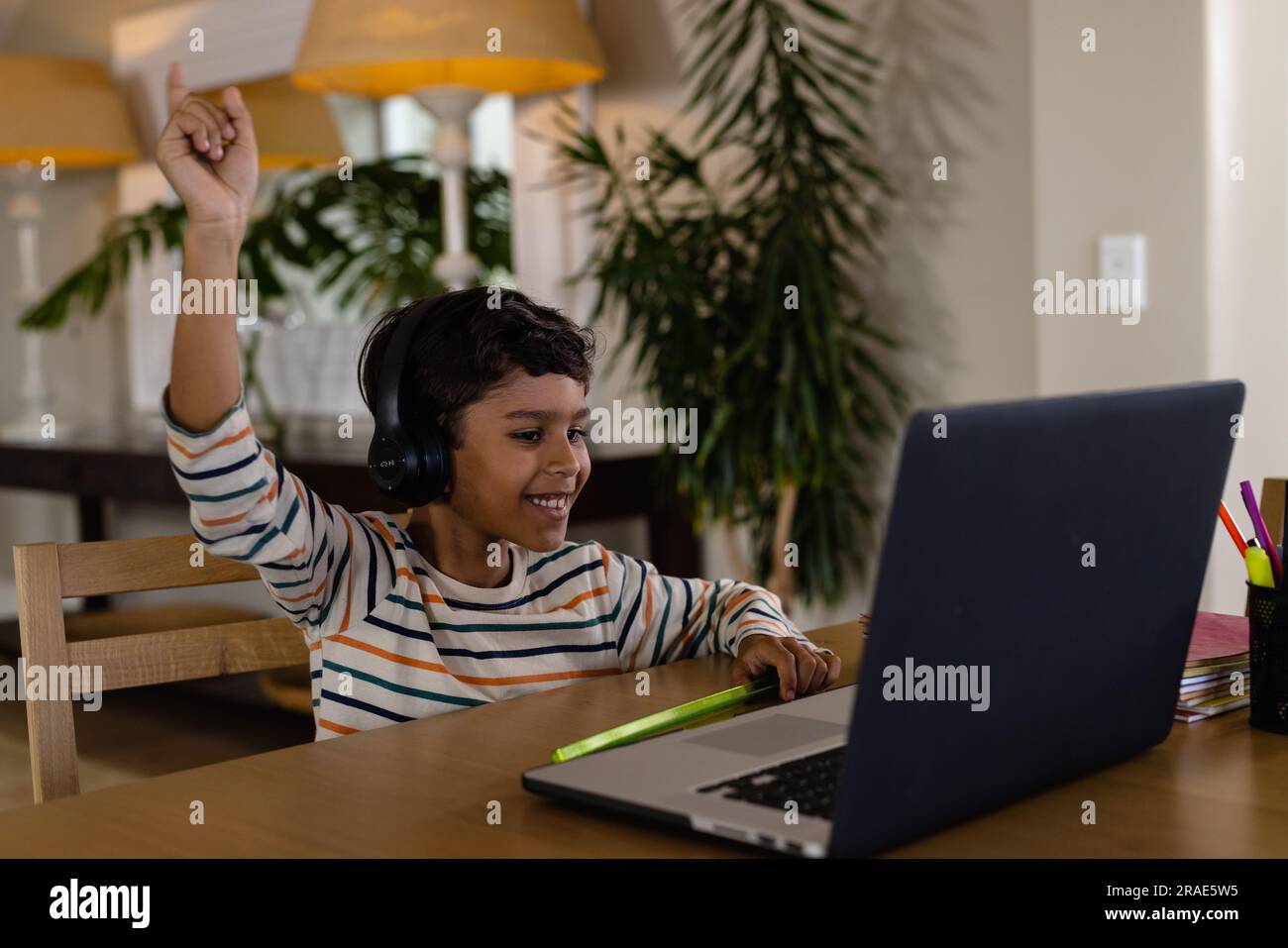 Happy biracial boy using headphones and laptop for online lesson at ...