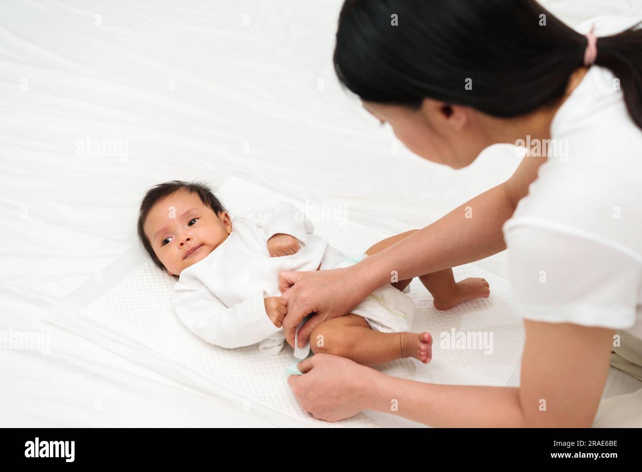 mother changing diaper of newborn baby while lying on a bed Stock Photo ...
