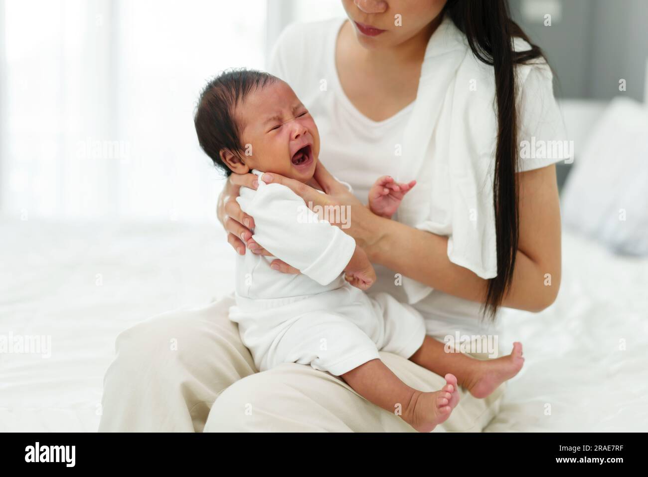 mother holding burping and crying baby in a bedroom after feeding milk ...