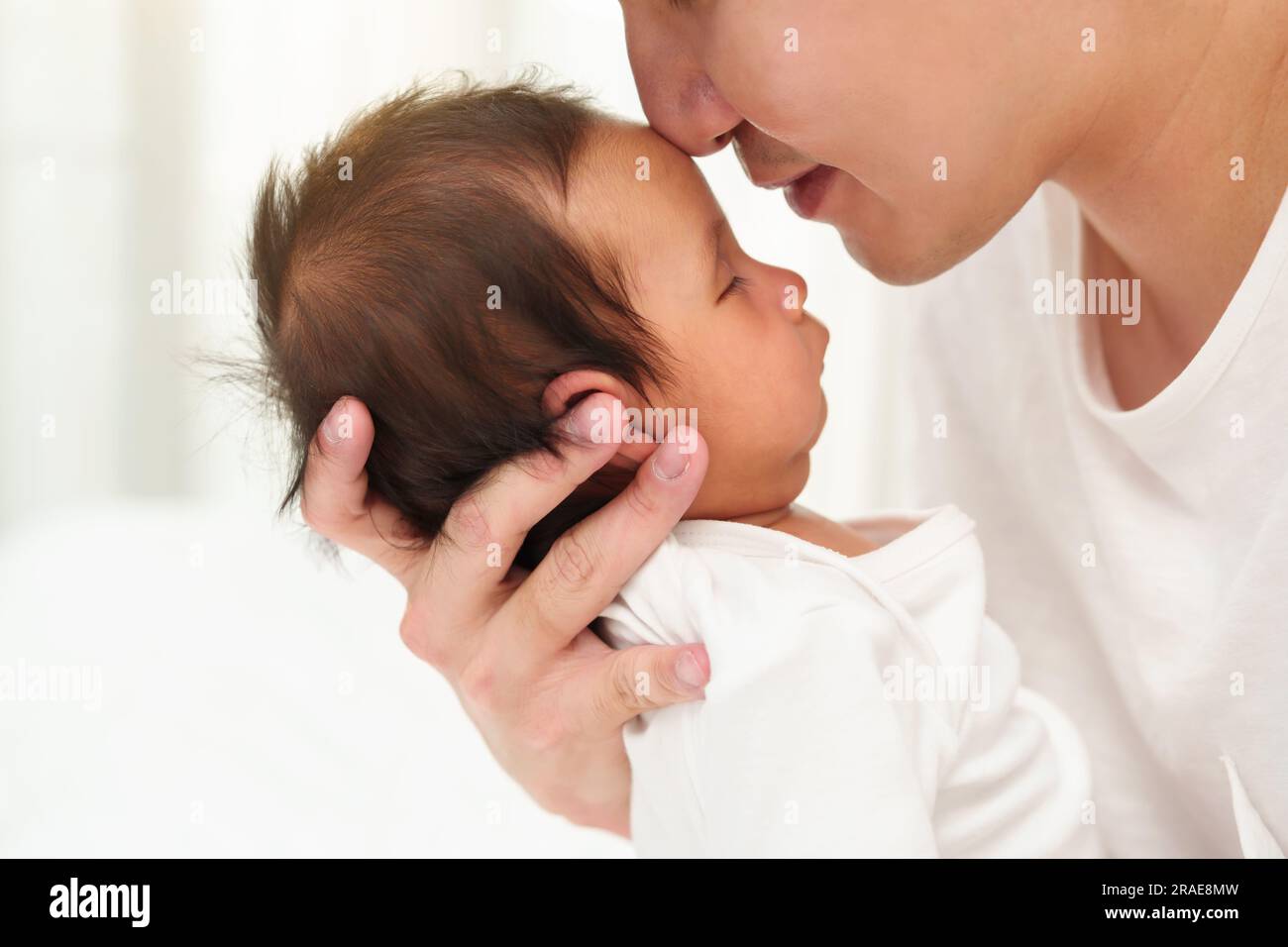 father kissing forehead of his newborn baby on a bed Stock Photo - Alamy