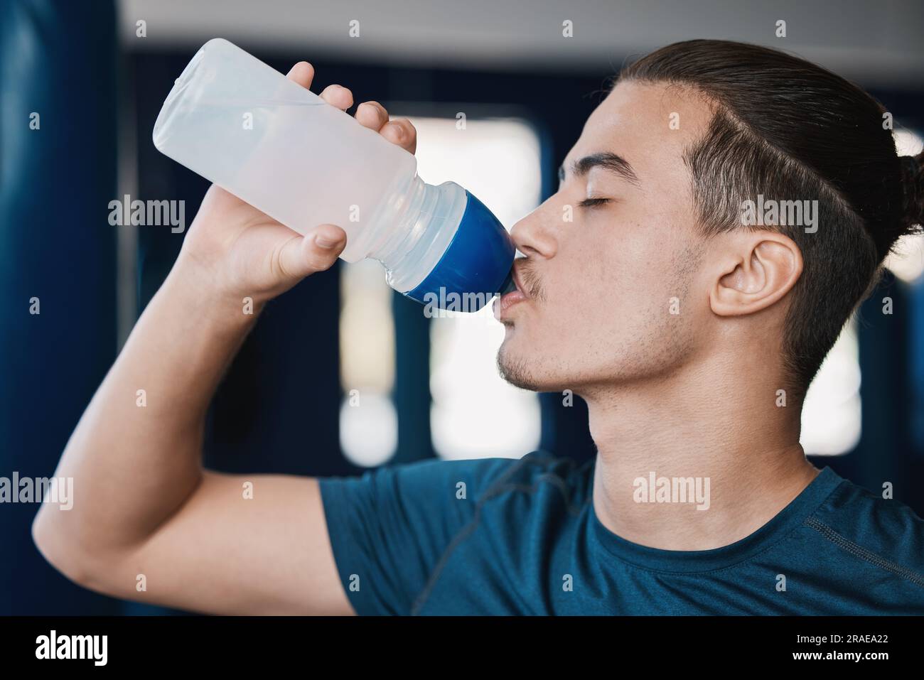 Thirsty, fitness and a man drinking water after exercise at the gym for ...