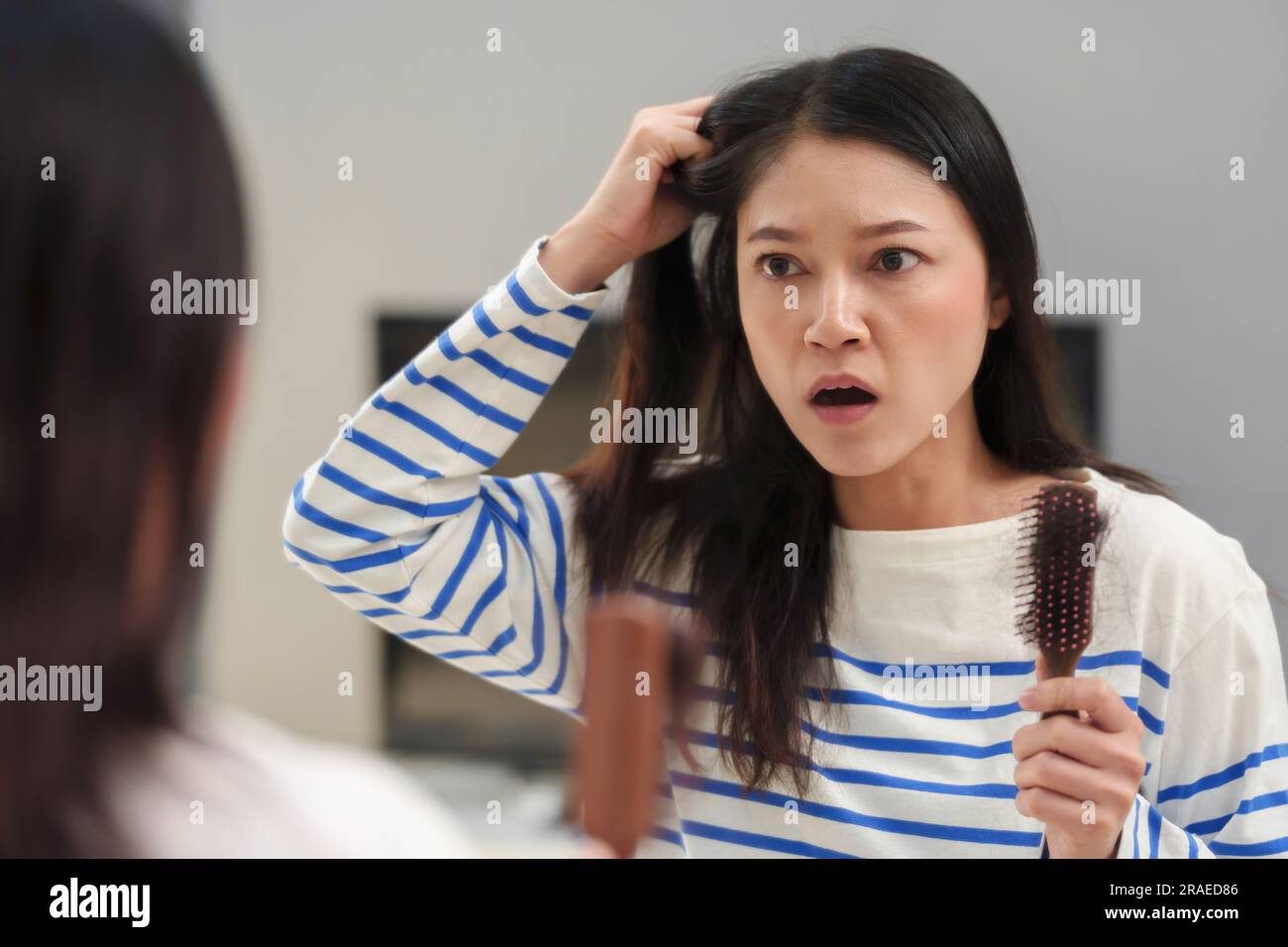shocked woman suffering hair loss problem with her hairbrush in mirror ...