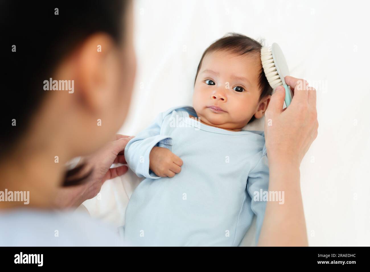mother combing her newborn baby hair on a bed Stock Photo - Alamy