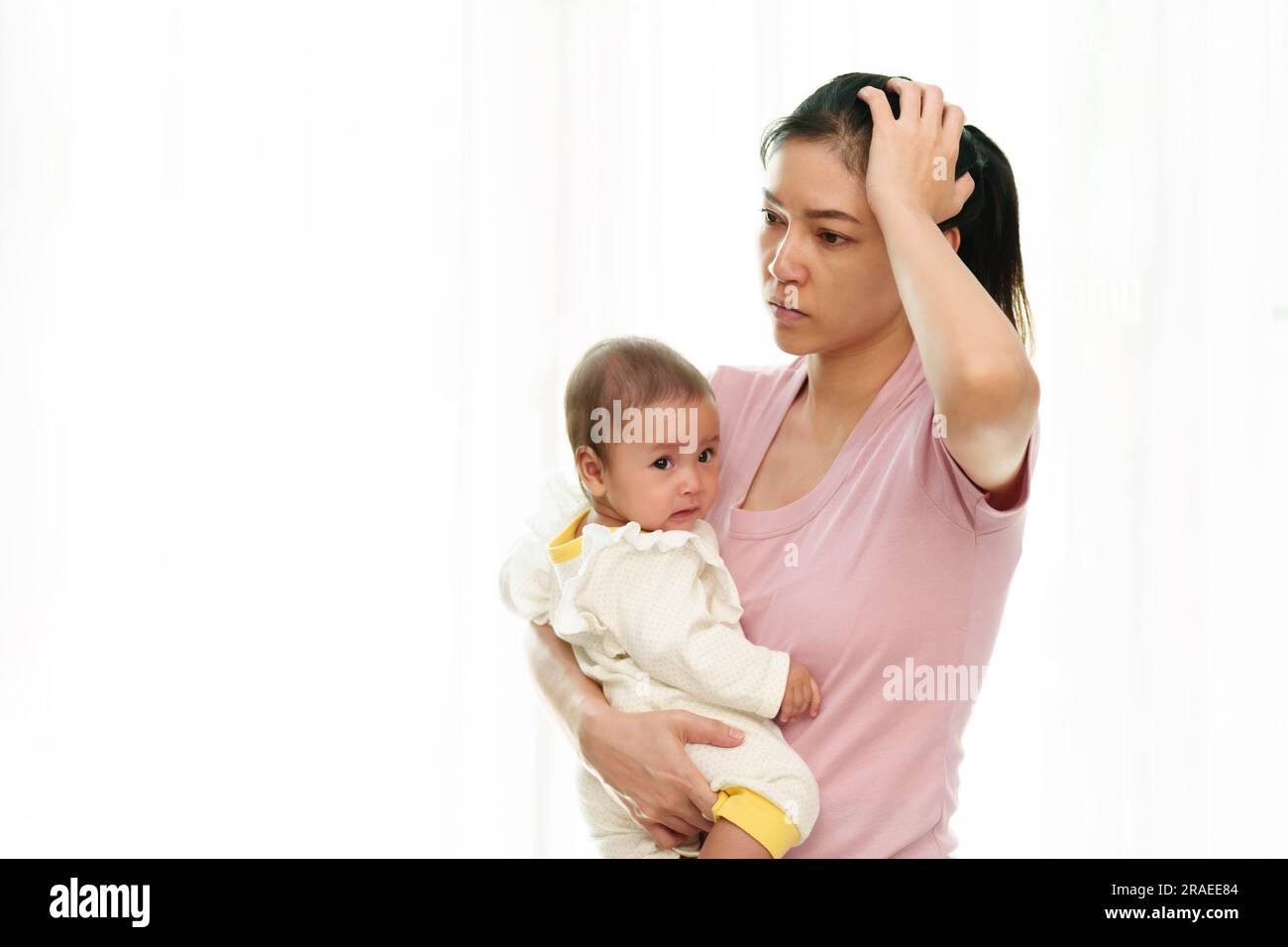 stressed mother holding with her infant baby on a window background ...